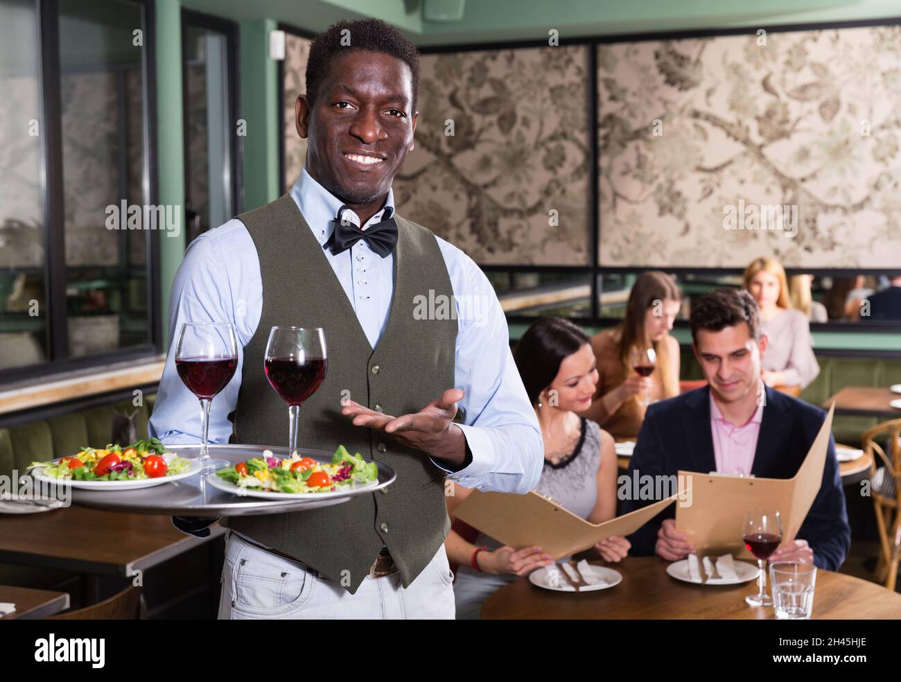 Hospitable African American waiter standing with serving tray ...