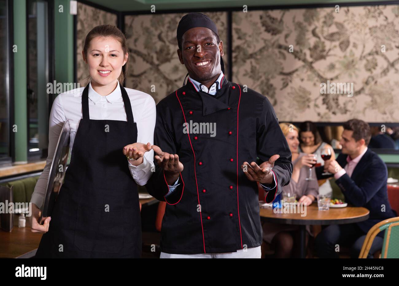 Polite waitress standing in restaurant hall with cheerful African ...