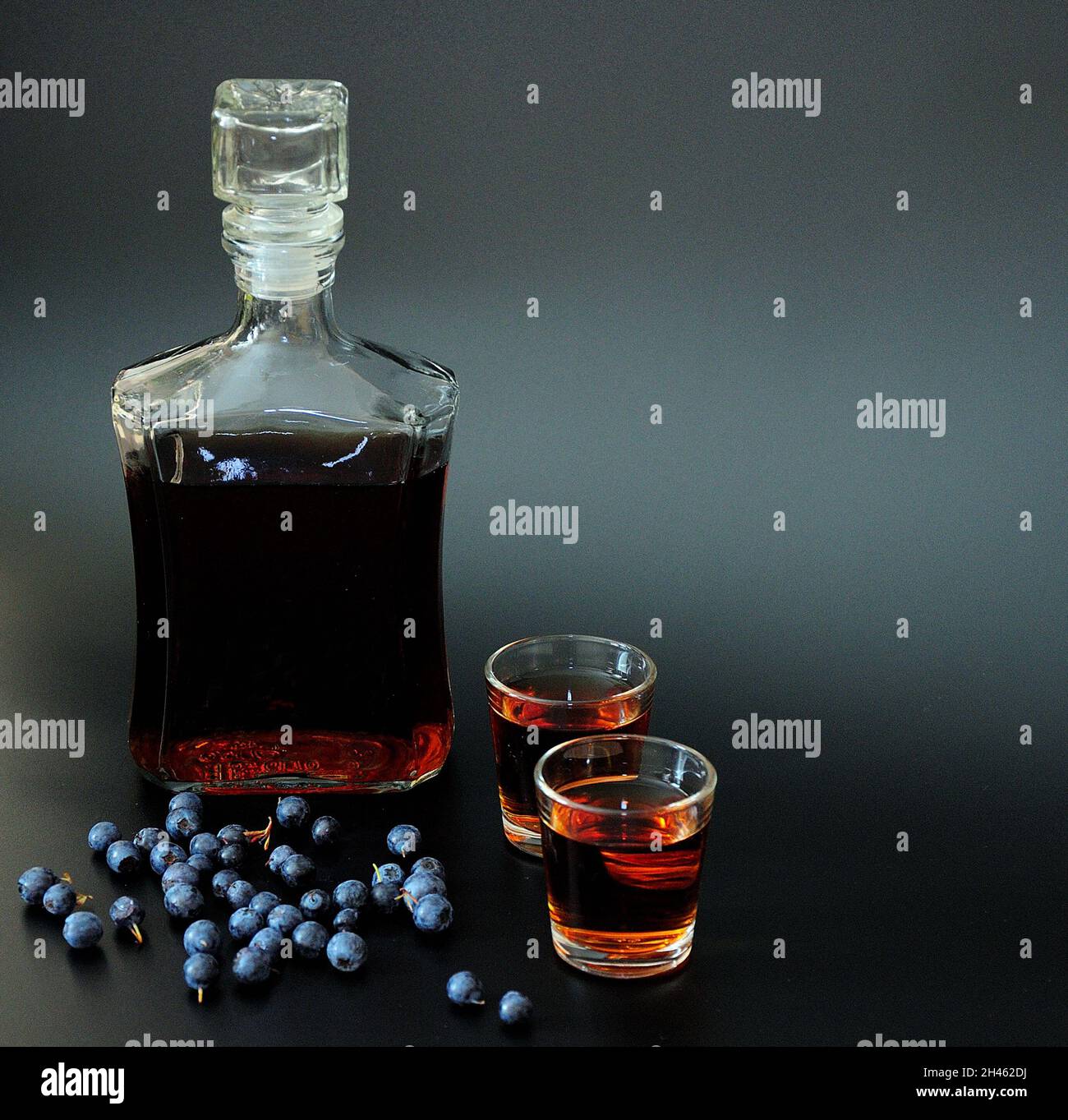 Homemade blueberry liqueur, strong alcohol in two glasses and a glass decanter on a black ...