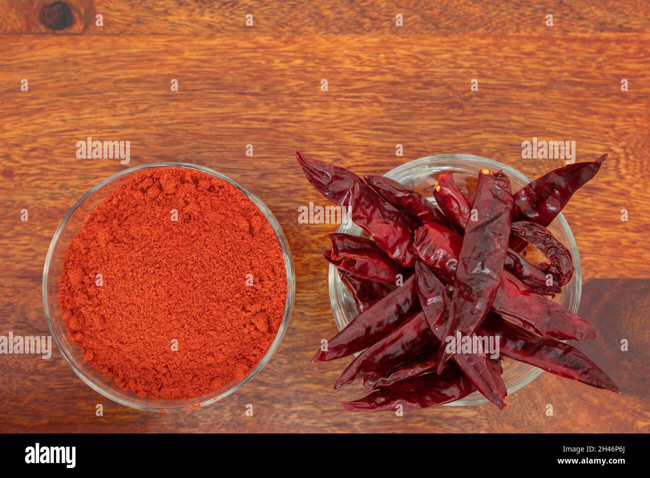 Top view of dry red chillies and red chilli powder bowls kept side by ...