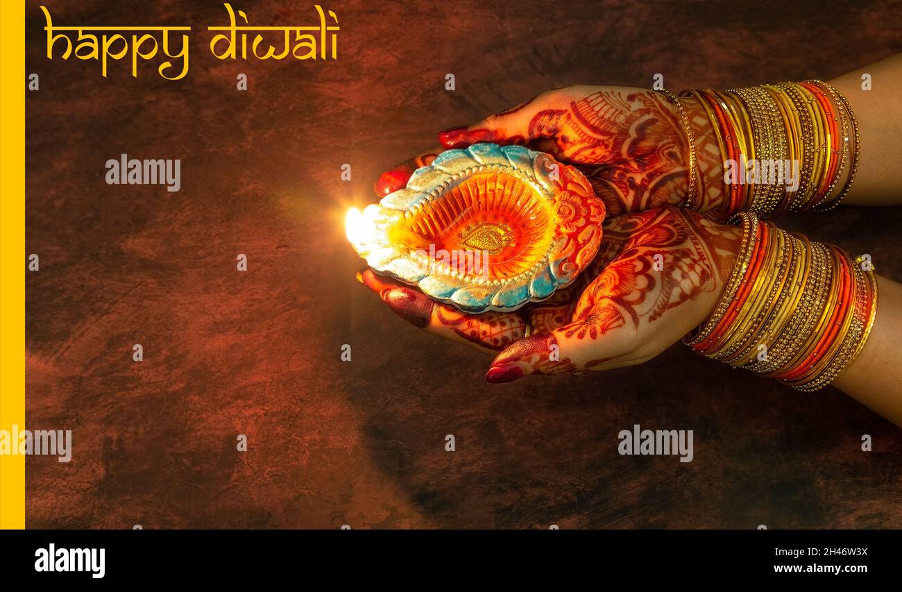 Woman hand wearing mehndi and bangles in close up holding a Diwali Diya ...
