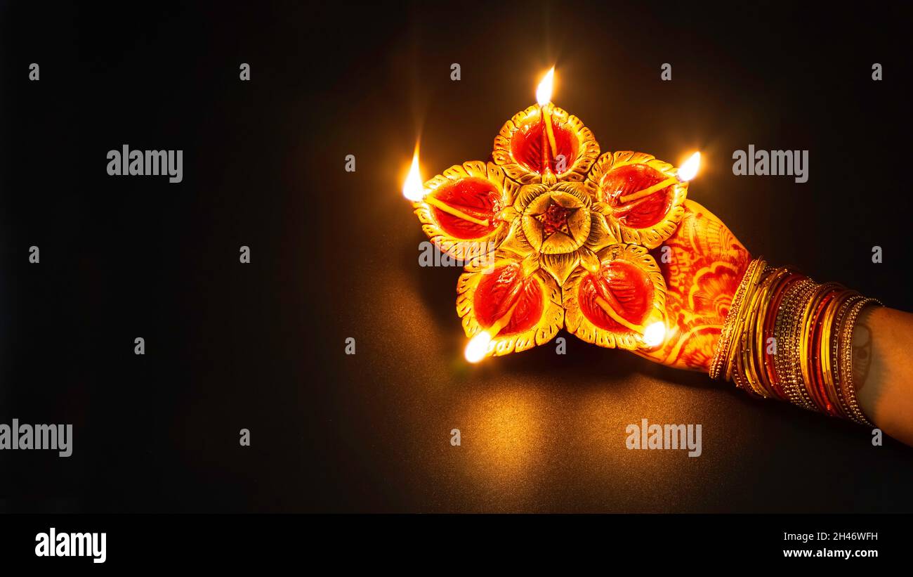 Woman hand wearing mehndi and bangles in close up holding a Diwali Diya ...