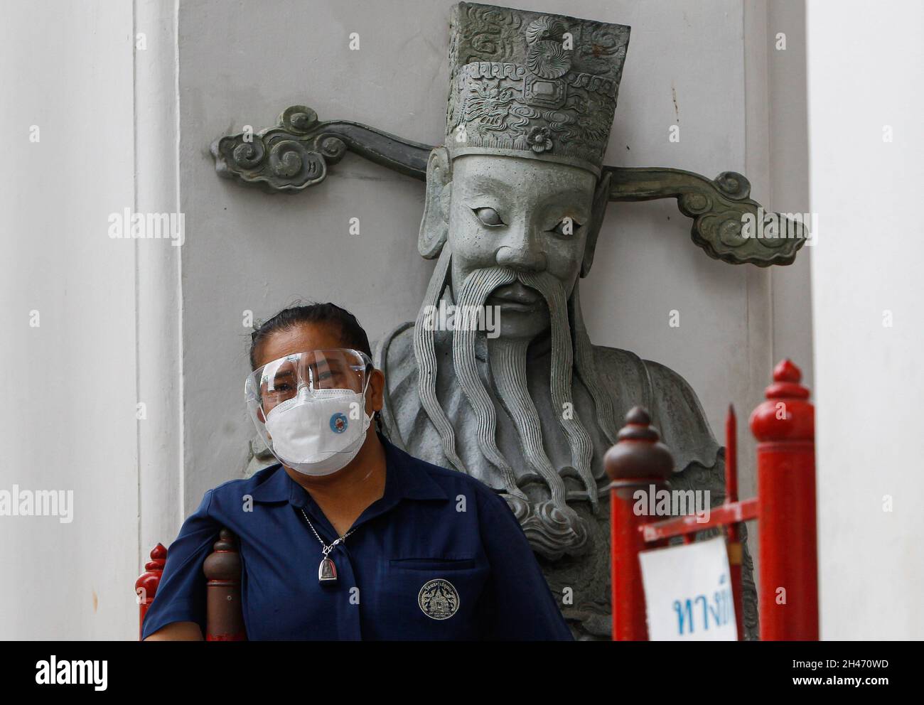 A man wearing a face mask stands in front of a Chinese statue at Wat ...