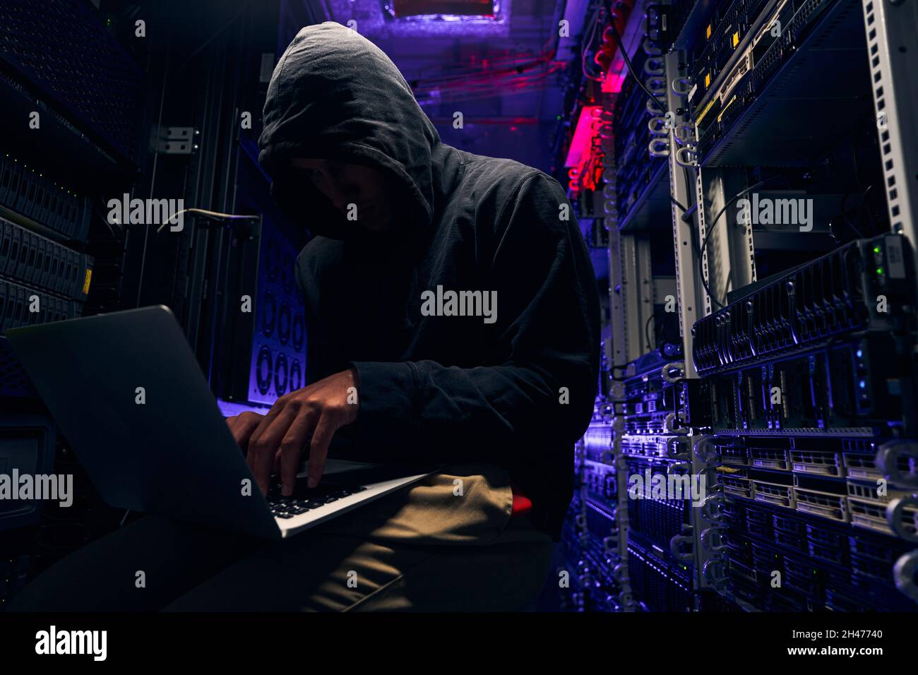 Hacker seated in server room launching cyberattack on laptop Stock ...