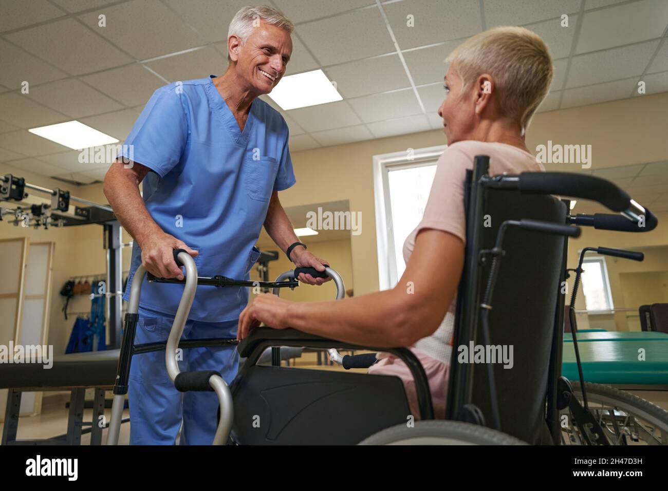 Healthcare professional helping mature woman to use walker in clinic ...