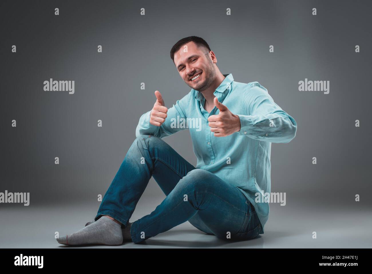 Handsome young man sitting on a floor with raised hands gesturing ...