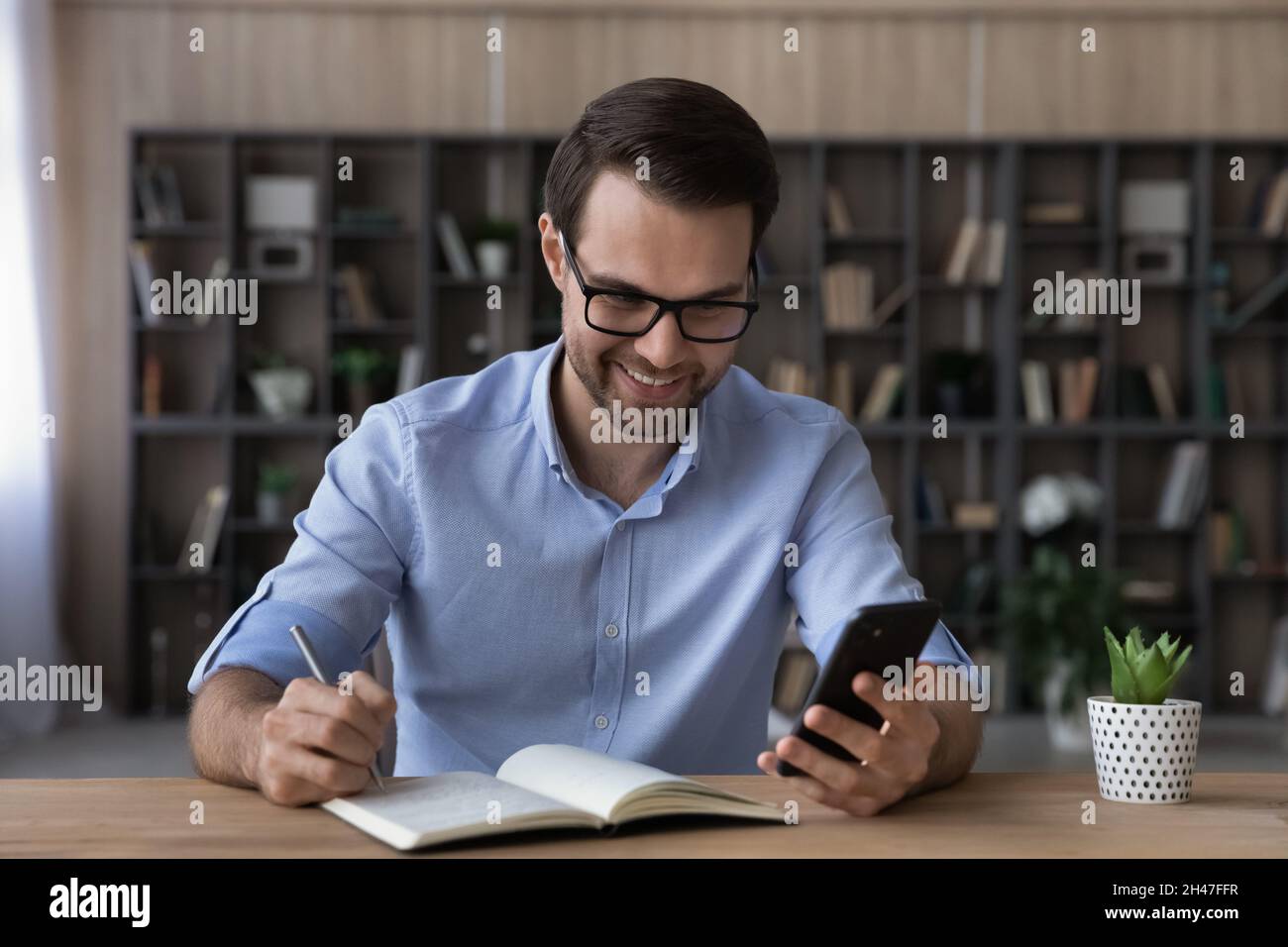 Happy young business man writing notes using cellphone Stock Photo - Alamy