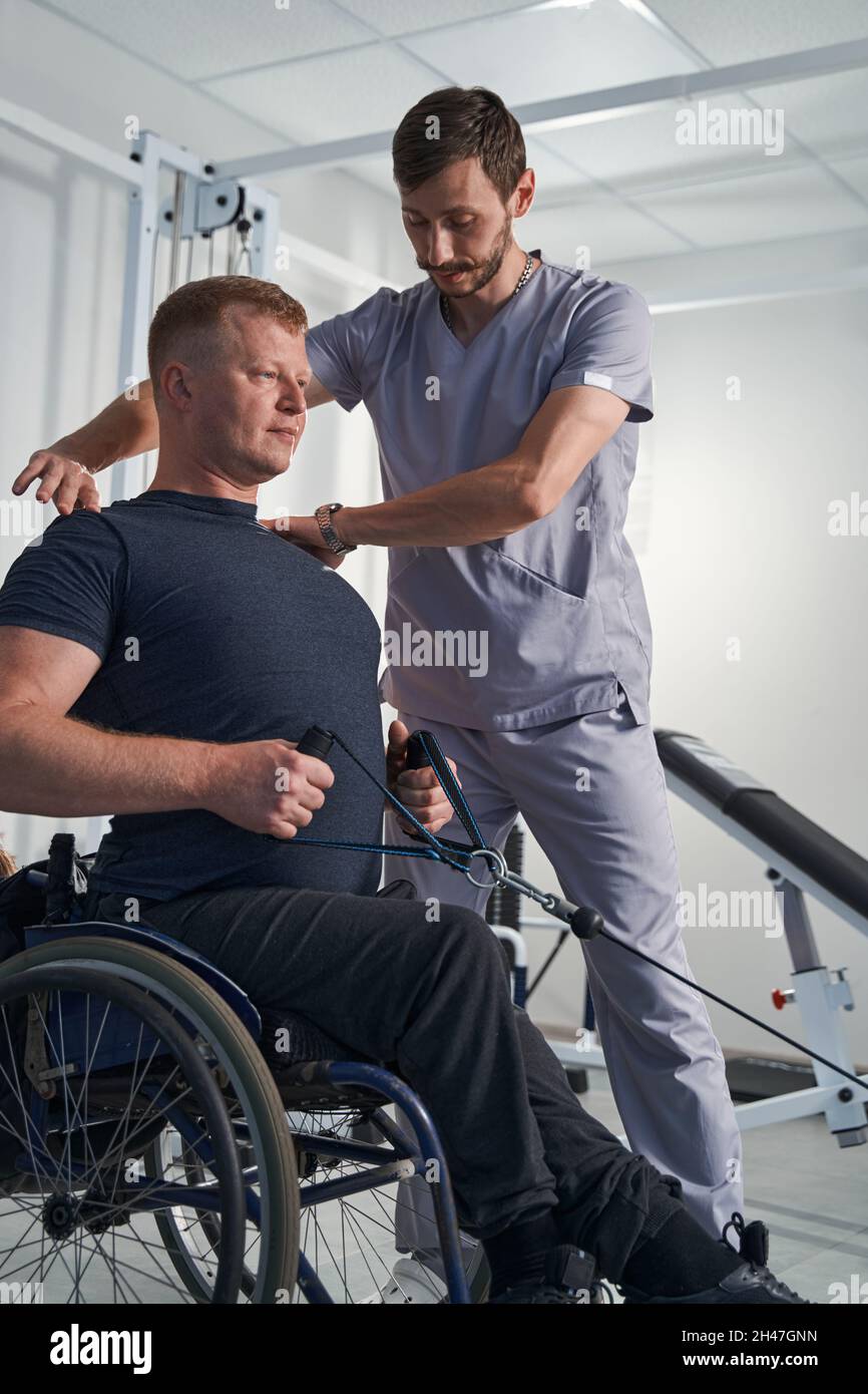 Doctor examining wheelchair patient shoulder pain. Checking posture ...