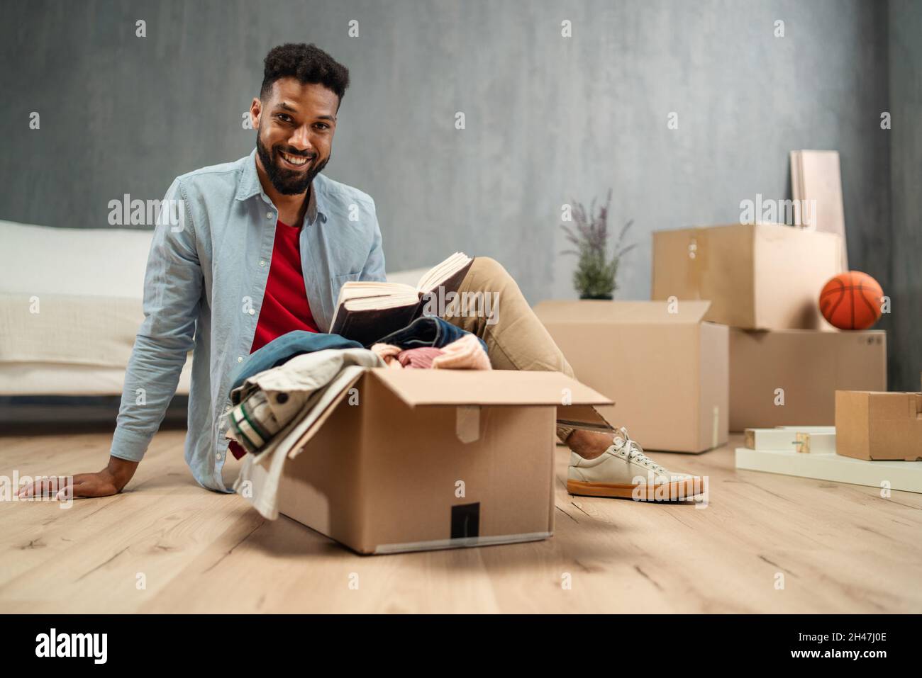 Happy young man putting clothes into packing boxes, moving home. new ...