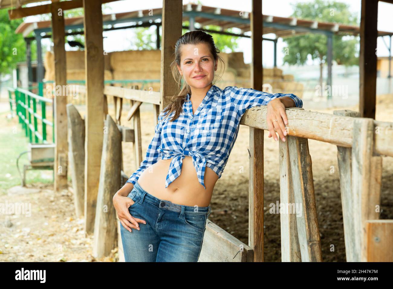 Happy confident young woman owner of ranch posing near empty stable on ...