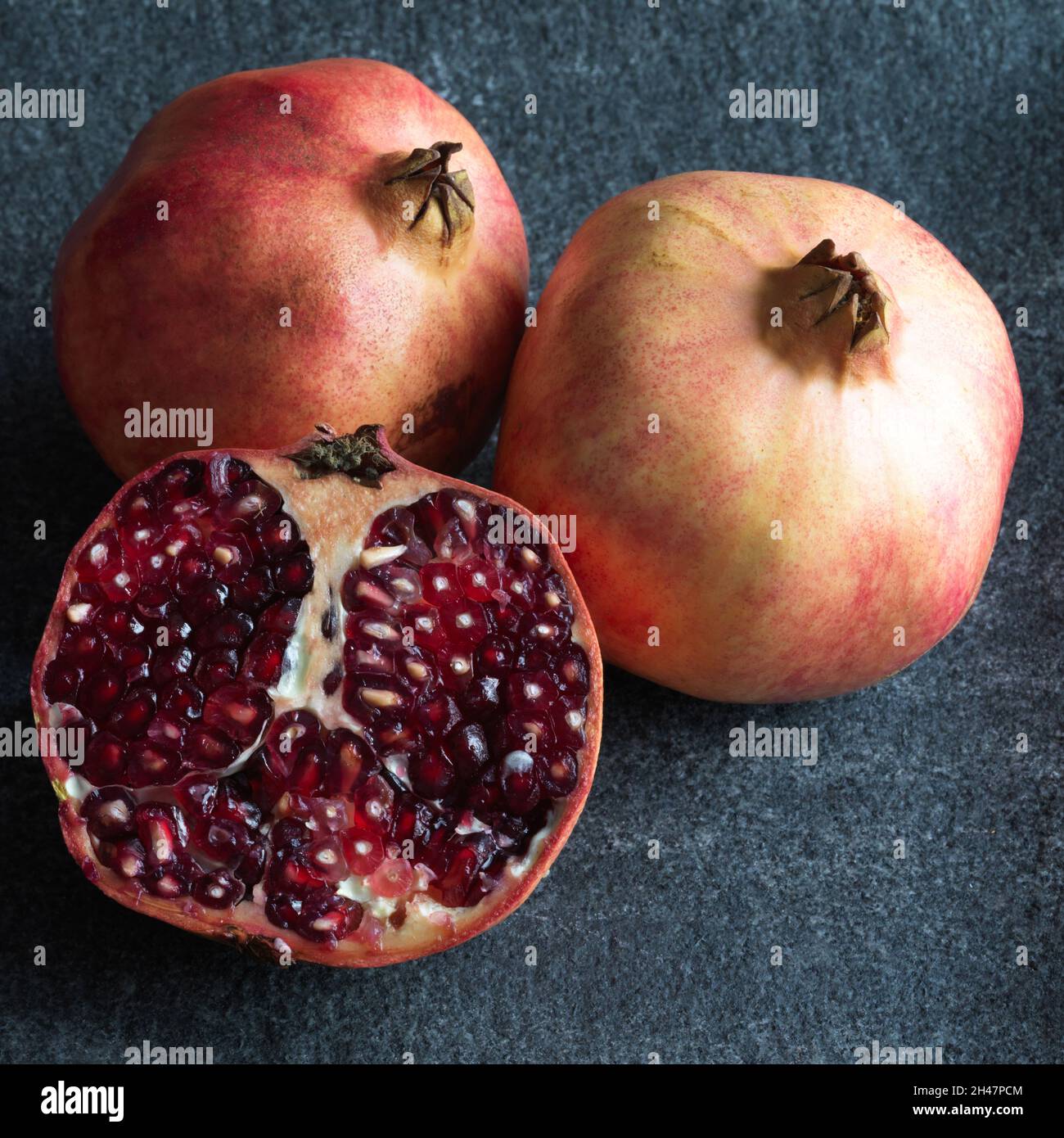 Three pomegranate on dark gray stone table, one cut open Stock Photo ...