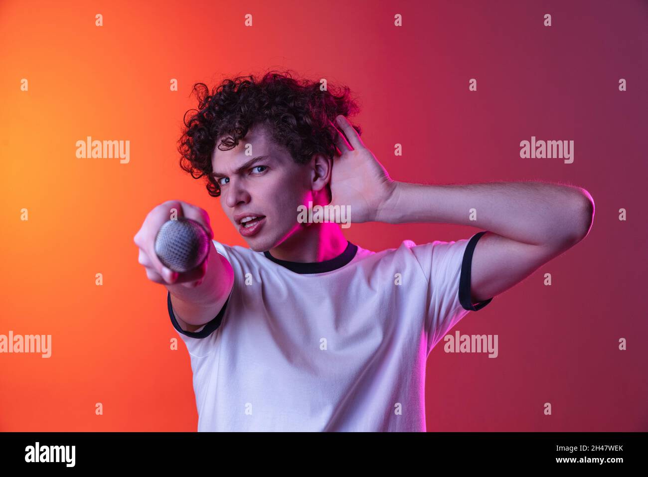 Cropped portrait of young man in white T-shirt directing microphone on ...