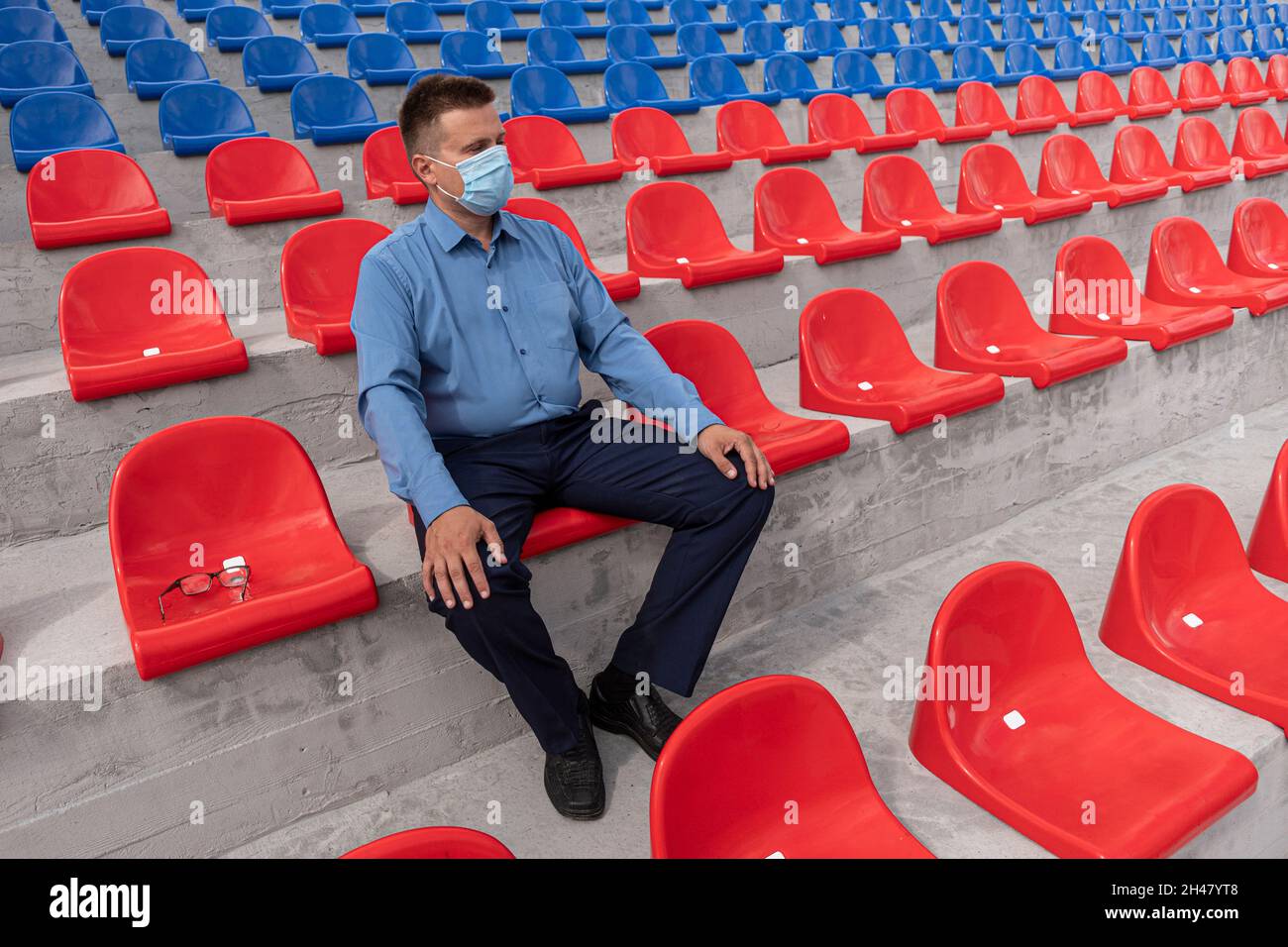 Football stands with red and blue plastic chairs. Football fan with a ...