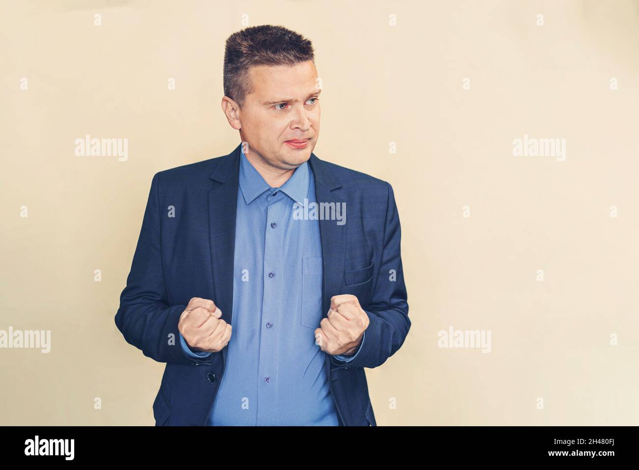 A young businessman in a blue suit clenched his hands into fists in an ...