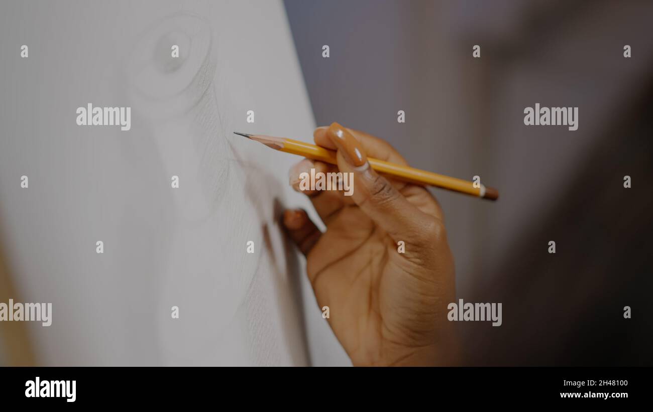 Close up of black hand with pencil drawing on white canvas and wooden ...