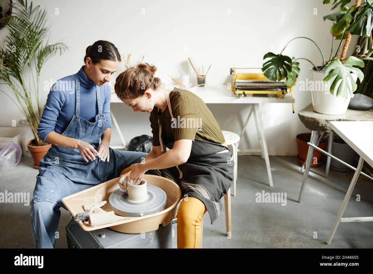 Portrait of two young women working on pottery wheel together in ...