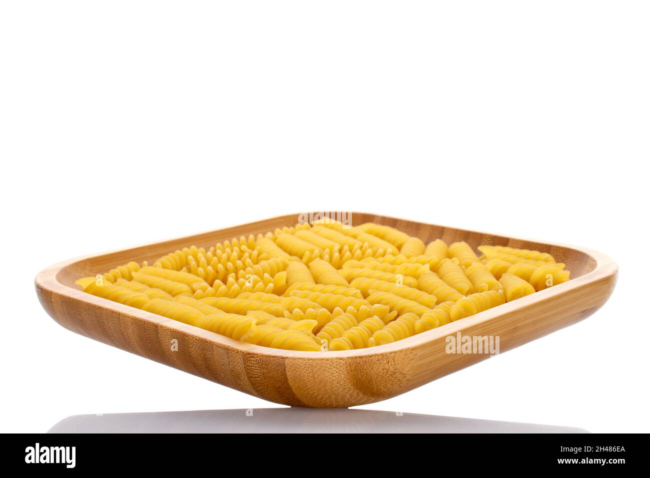 Bright yellow uncooked Fusilli pasta on a bamboo plate, close-up ...