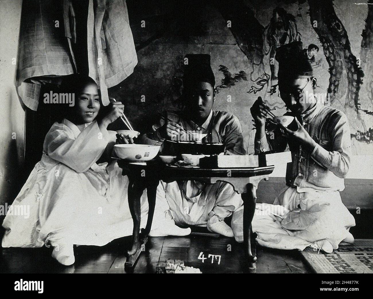 A group of people eating a meal, seated behind a small table, in front ...