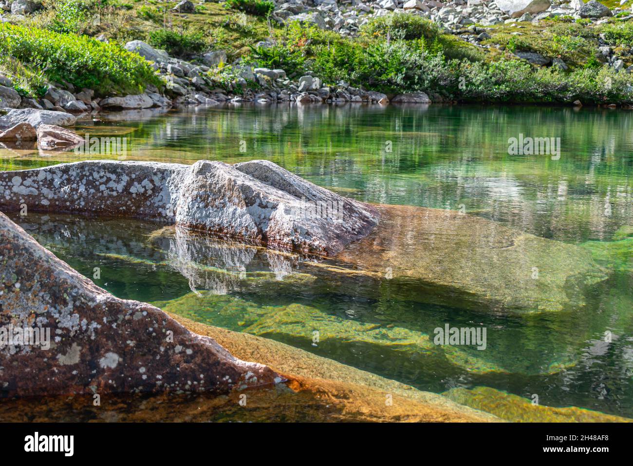 Green lake with clear transparent water from which huge granite stones ...