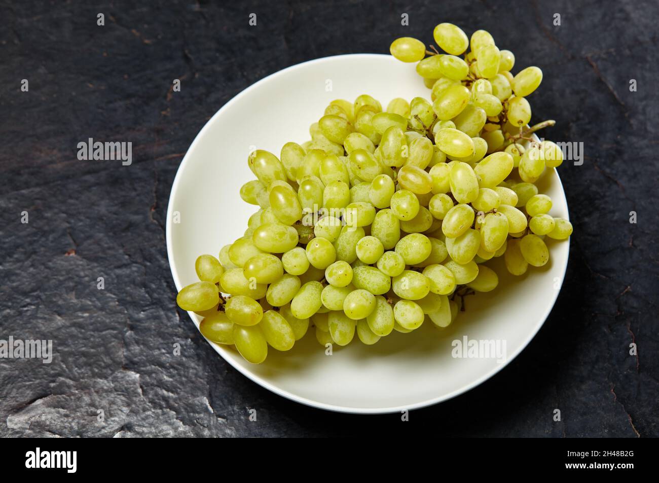 Branch of ripe grape on plate. Juicy grapes on wooden background, closeup. Grapes on dark ...