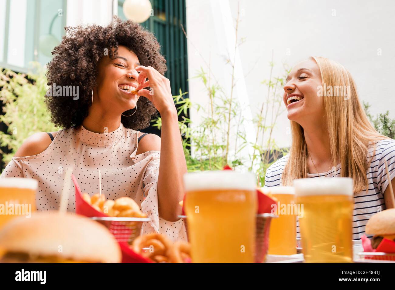 Two attractive vivacious young women enjoying snacks and a beer ...