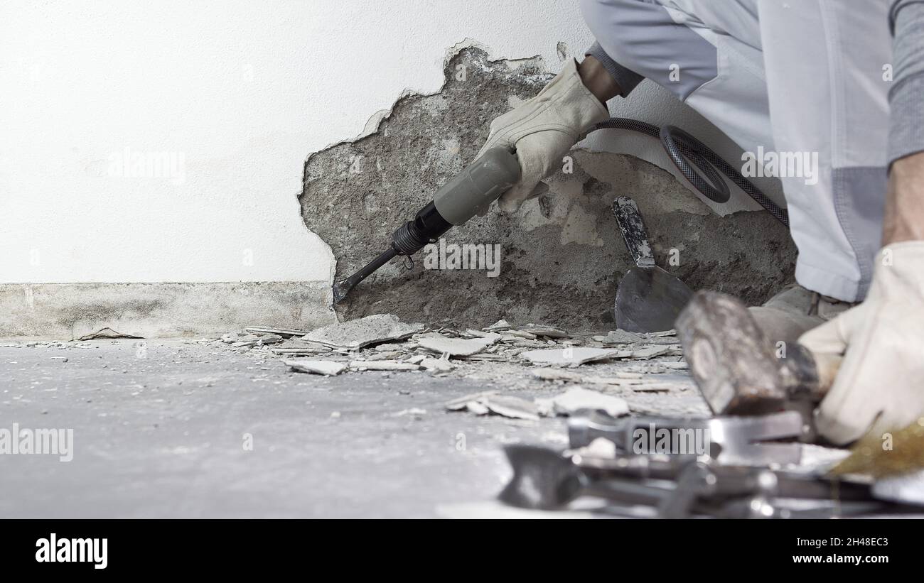 house renovation concept, construction worker breaks the old plaster of ...