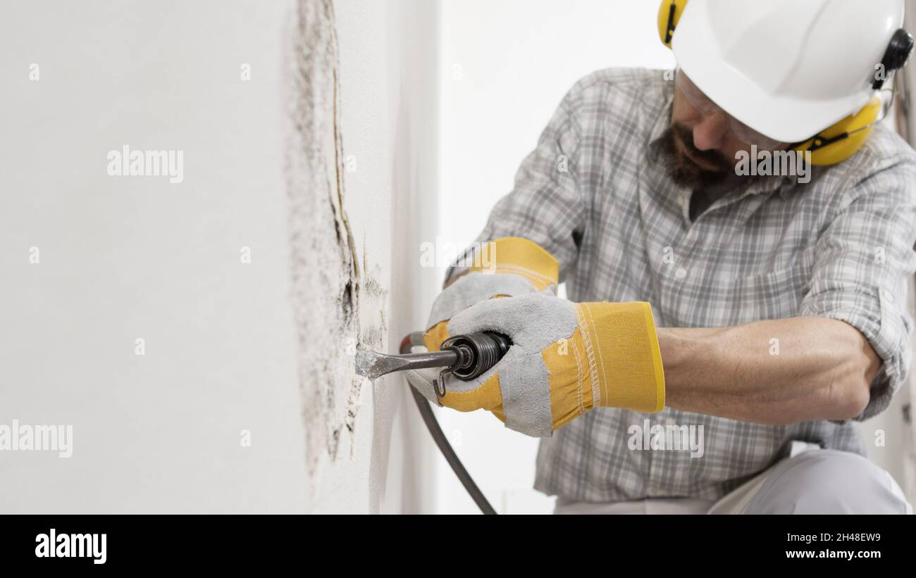 house renovation concept, construction worker breaks the old plaster of ...