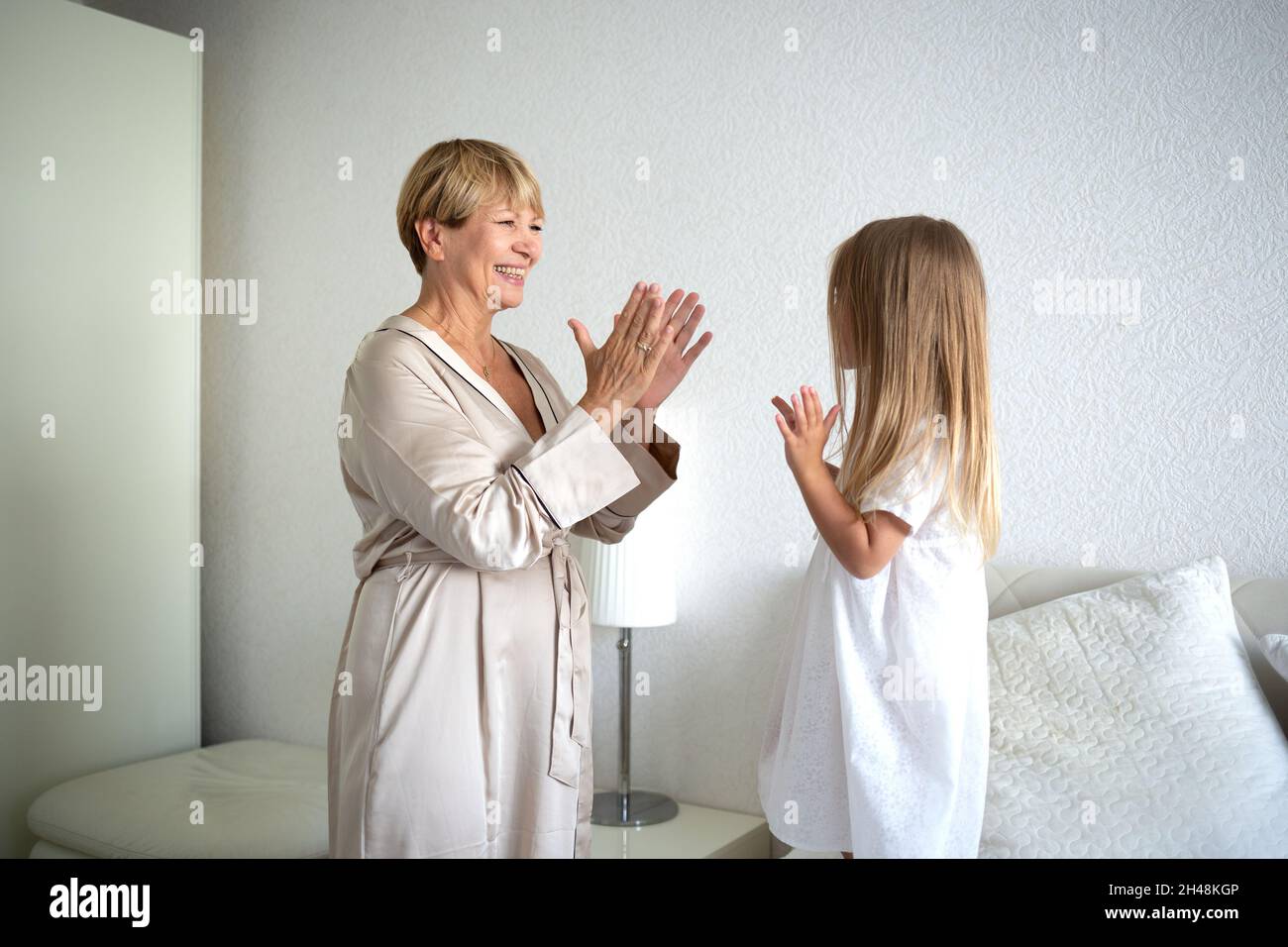 Little girl with grandmother clap their hands in the bedroom on the bed ...