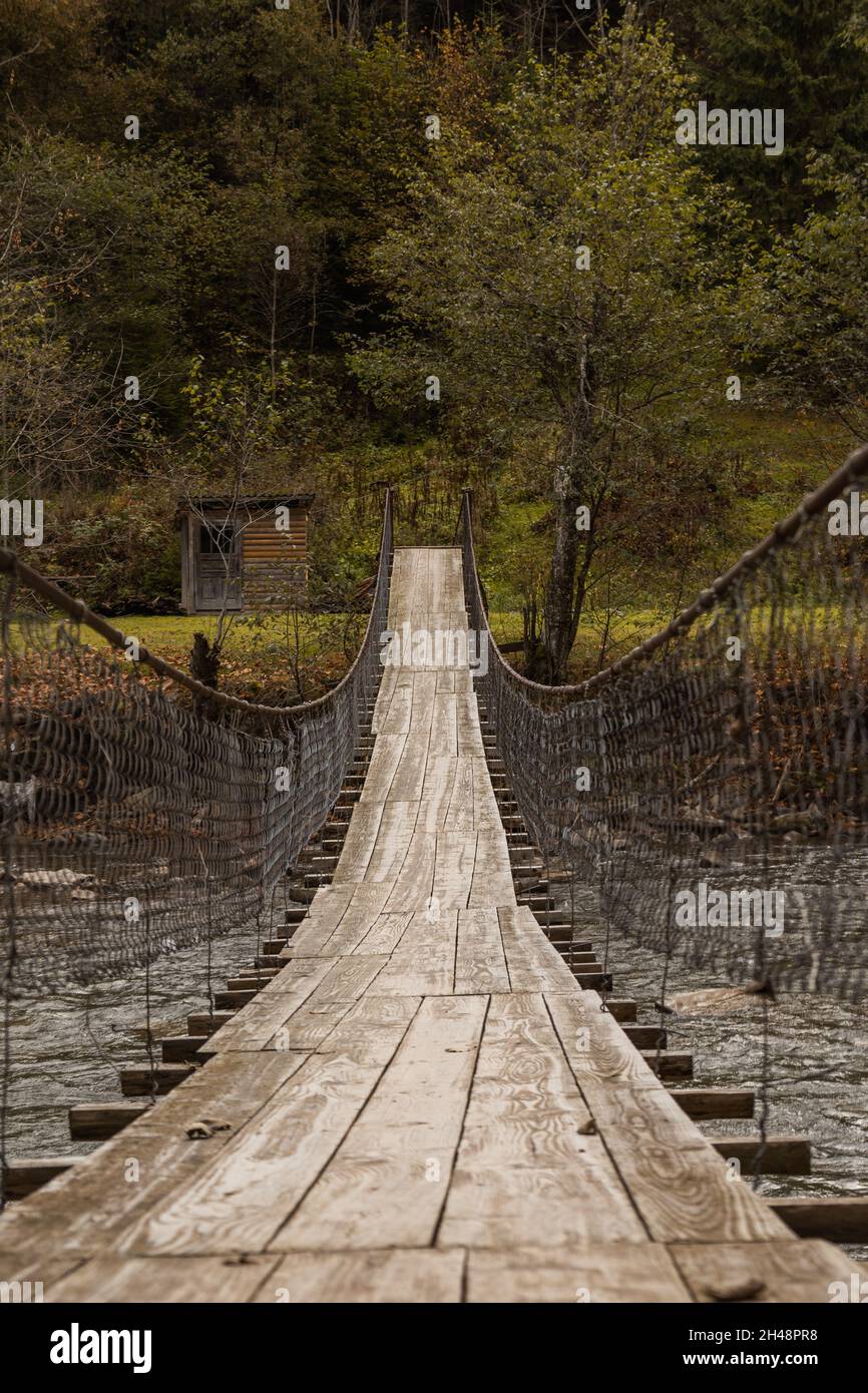 Old wooden suspension bridge across mountain river among autumn forest ...
