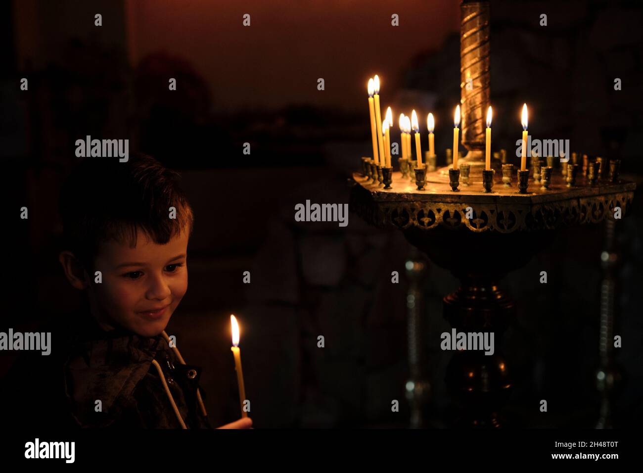 Little boy holding candle on dark background. A Child lights a candle ...