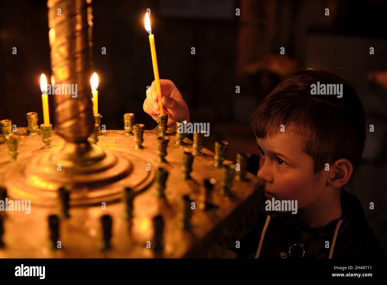 Little Boy lighting a church candle. A Child lights a candle in a ...