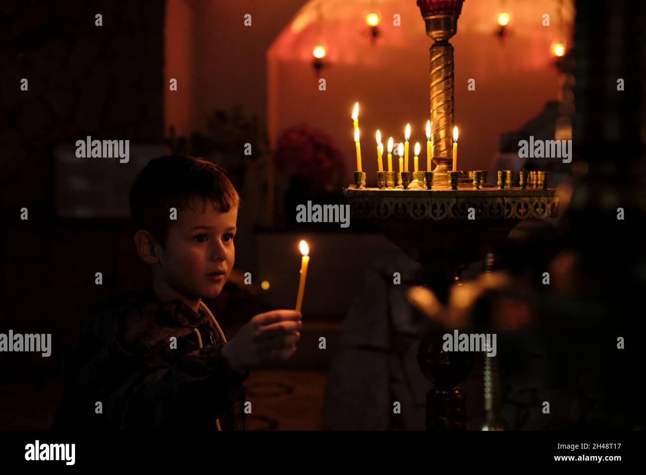 Little boy holding candle on dark background. A Child lights a candle ...