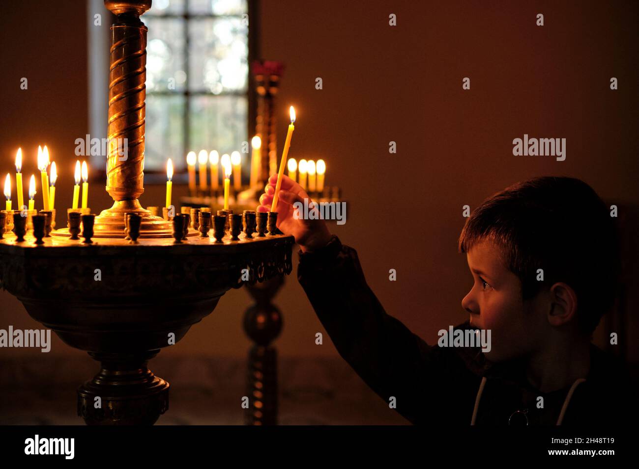 Little Boy lighting a church candle. A Child lights a candle in a ...