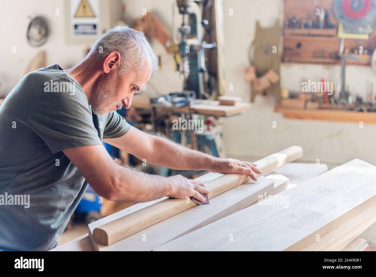 Standing senior man sanding wood with his arms Stock Photo - Alamy