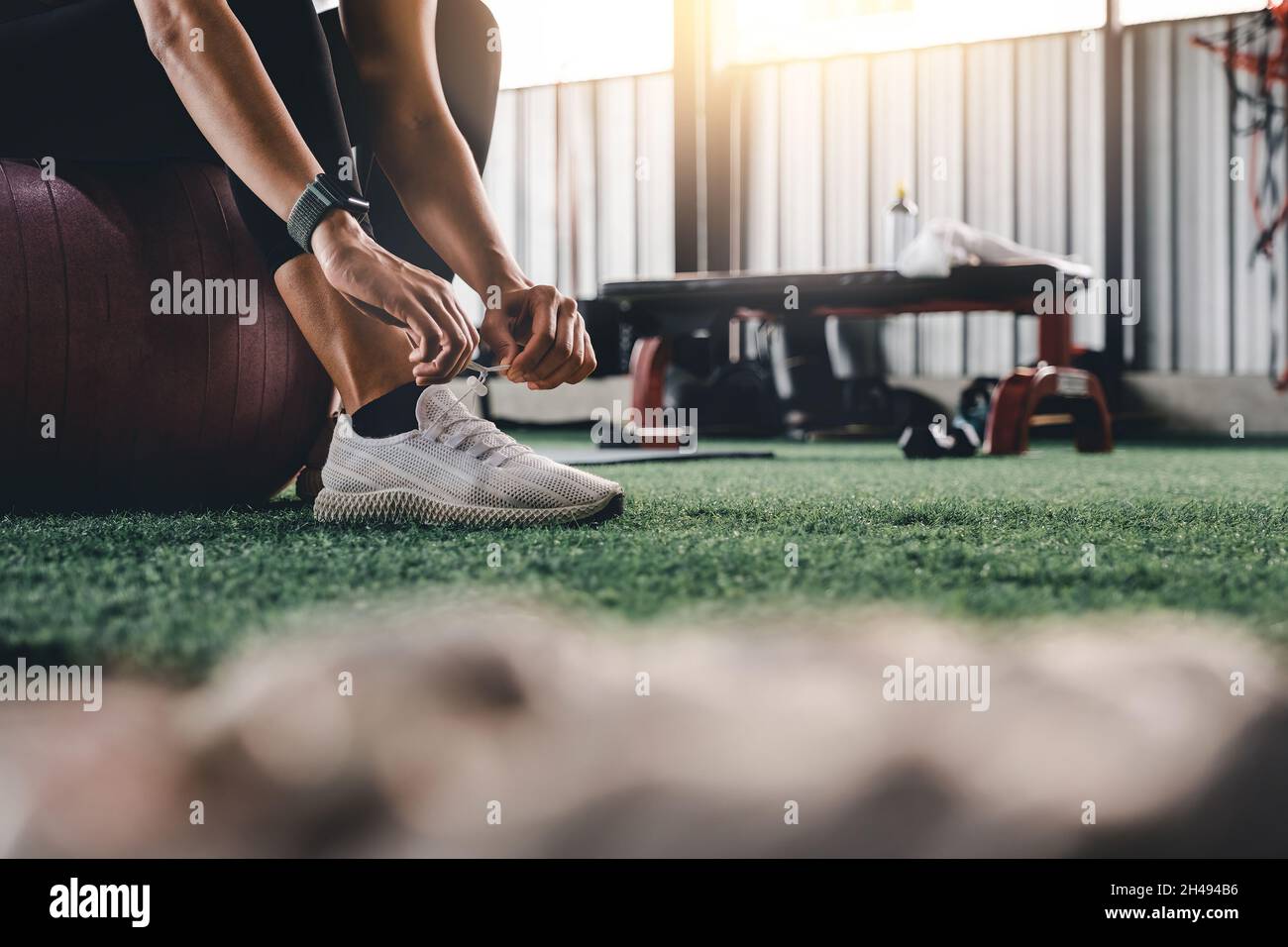 Woman sitting on gym ball tying shoelace and getting ready for fitness ...