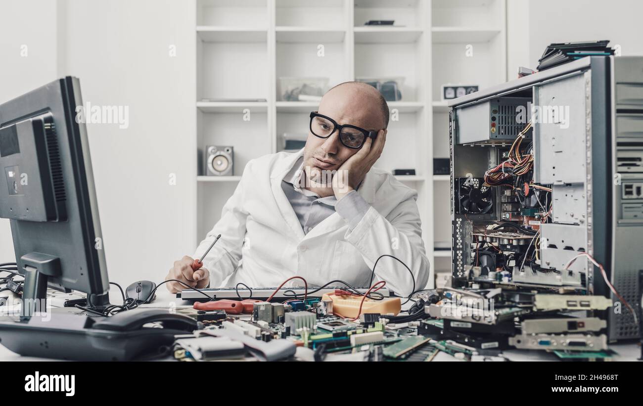 Frustrated exhausted technician trying to repair a computer, his desk ...