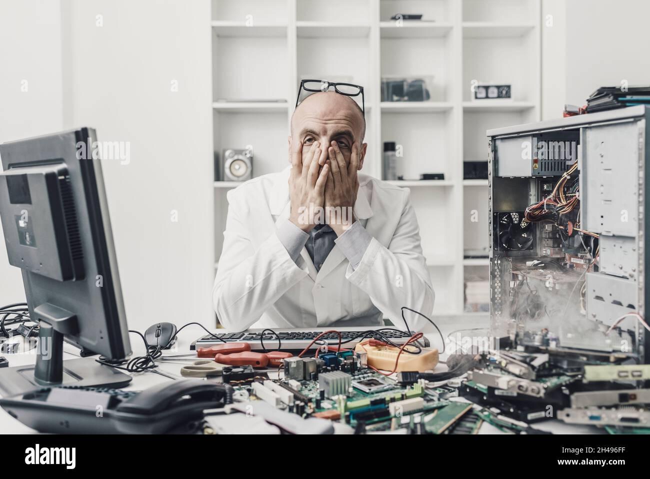 Frustrated exhausted technician trying to repair a computer, his desk ...