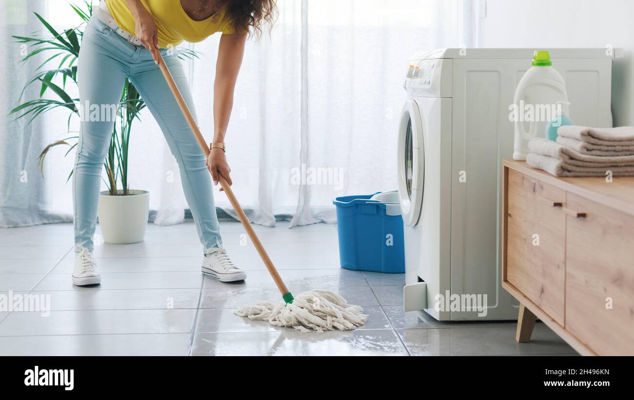Broken washing machine leaking on the floor, a woman is cleaning with a ...