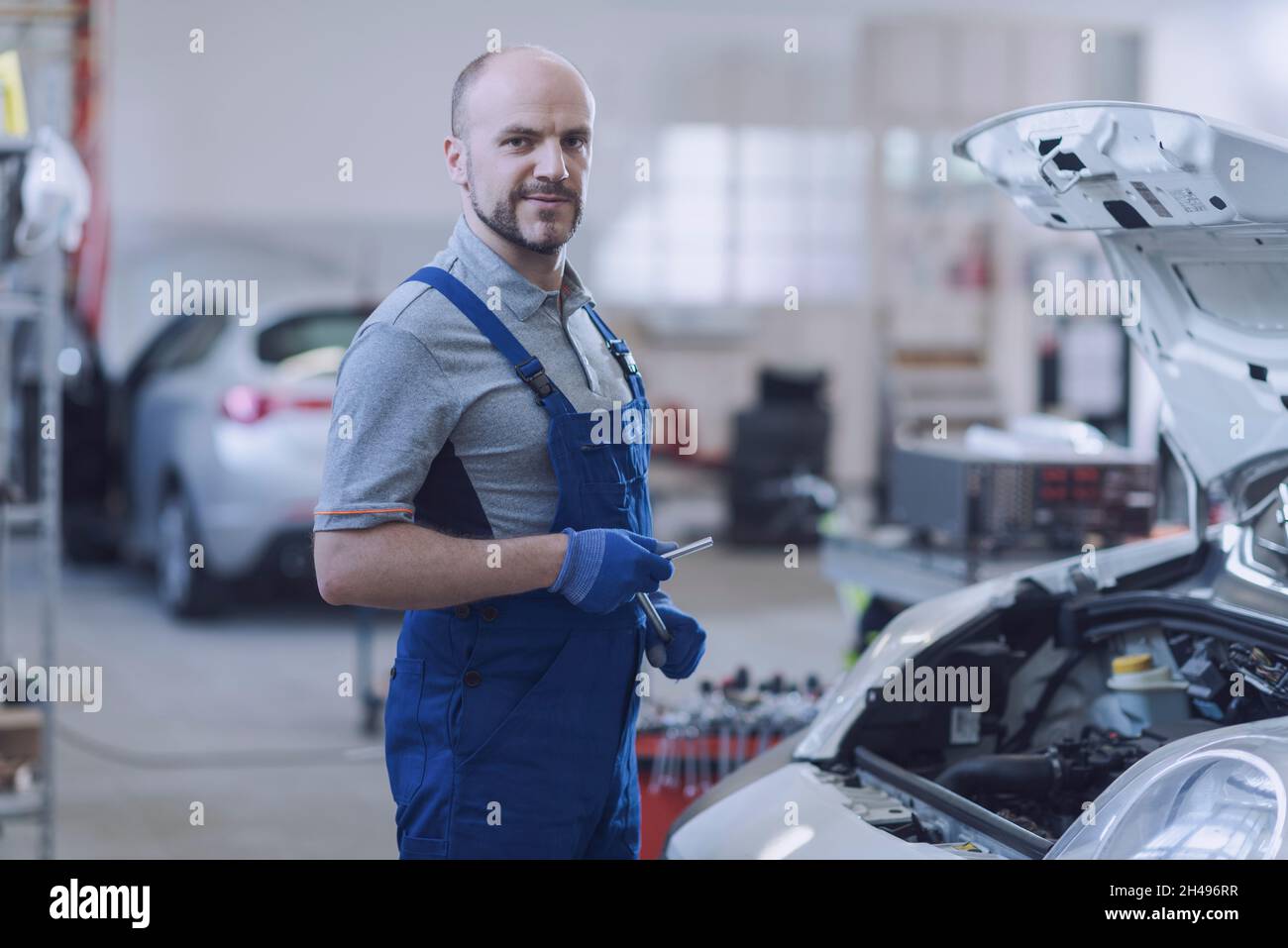 Confident mechanic posing in the garage, he is checking a car engine ...