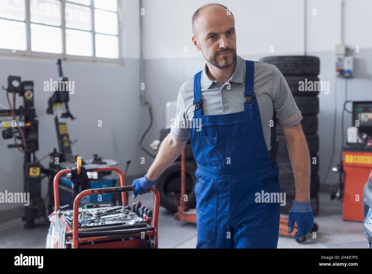 Mechanic working in the auto repair shop, he is pulling a tool cart ...
