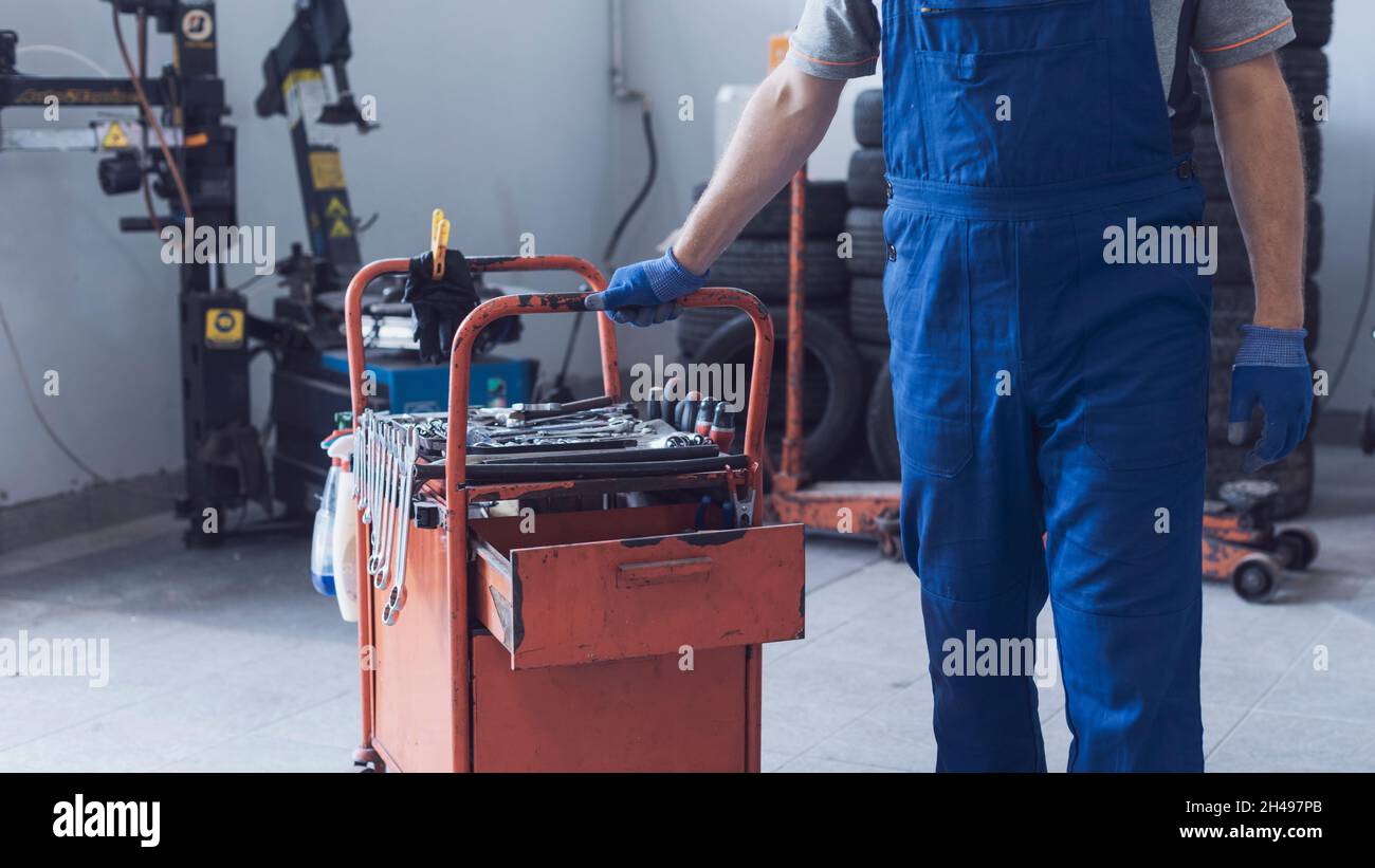 Mechanic working in the auto repair shop, he is pulling a tool cart ...