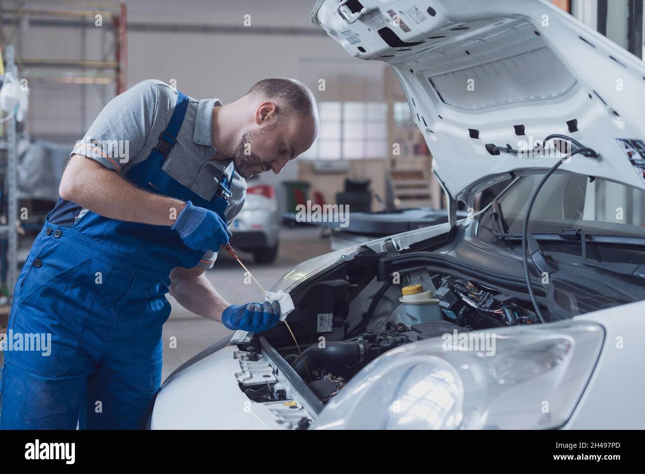 Mechanic doing a vehicle inspection, he is checking a car's oil level ...