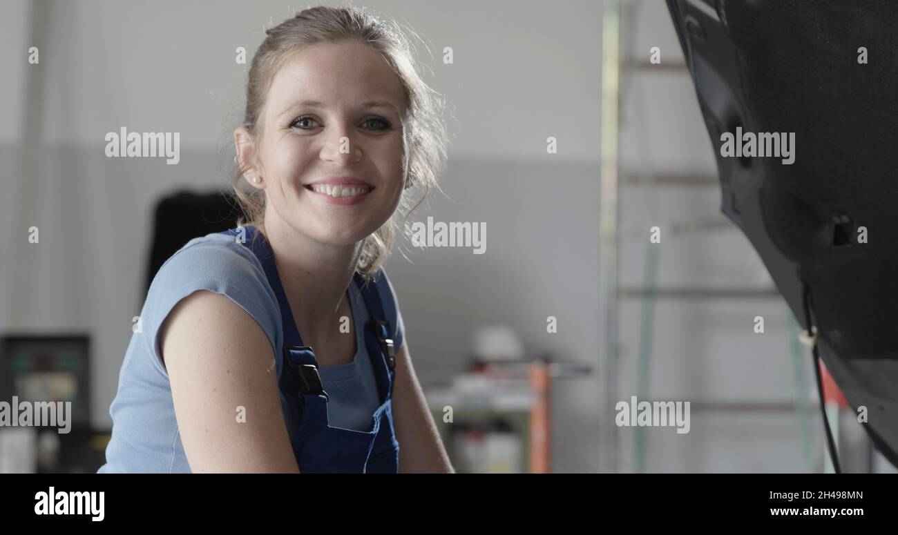 Beautiful female mechanic in the car workshop, she is smiling at camera ...