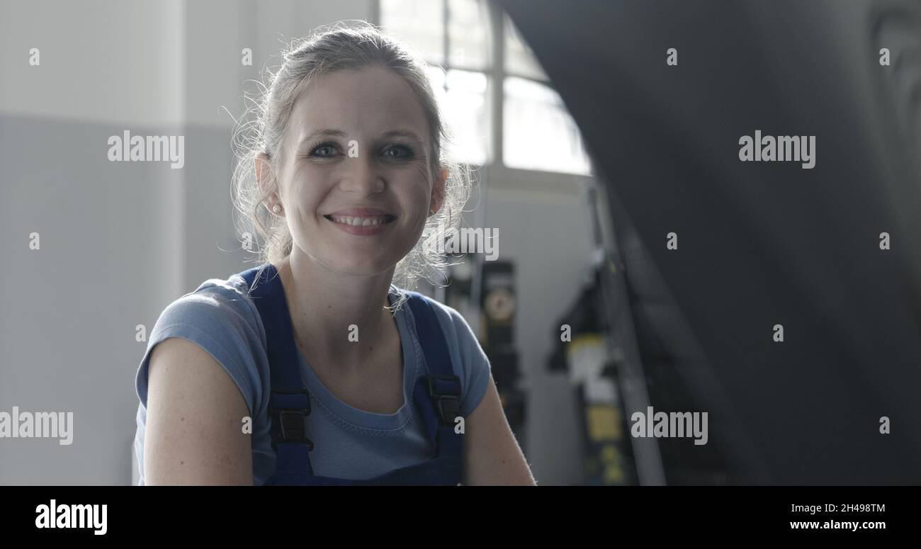 Beautiful female mechanic in the car workshop, she is smiling at camera ...