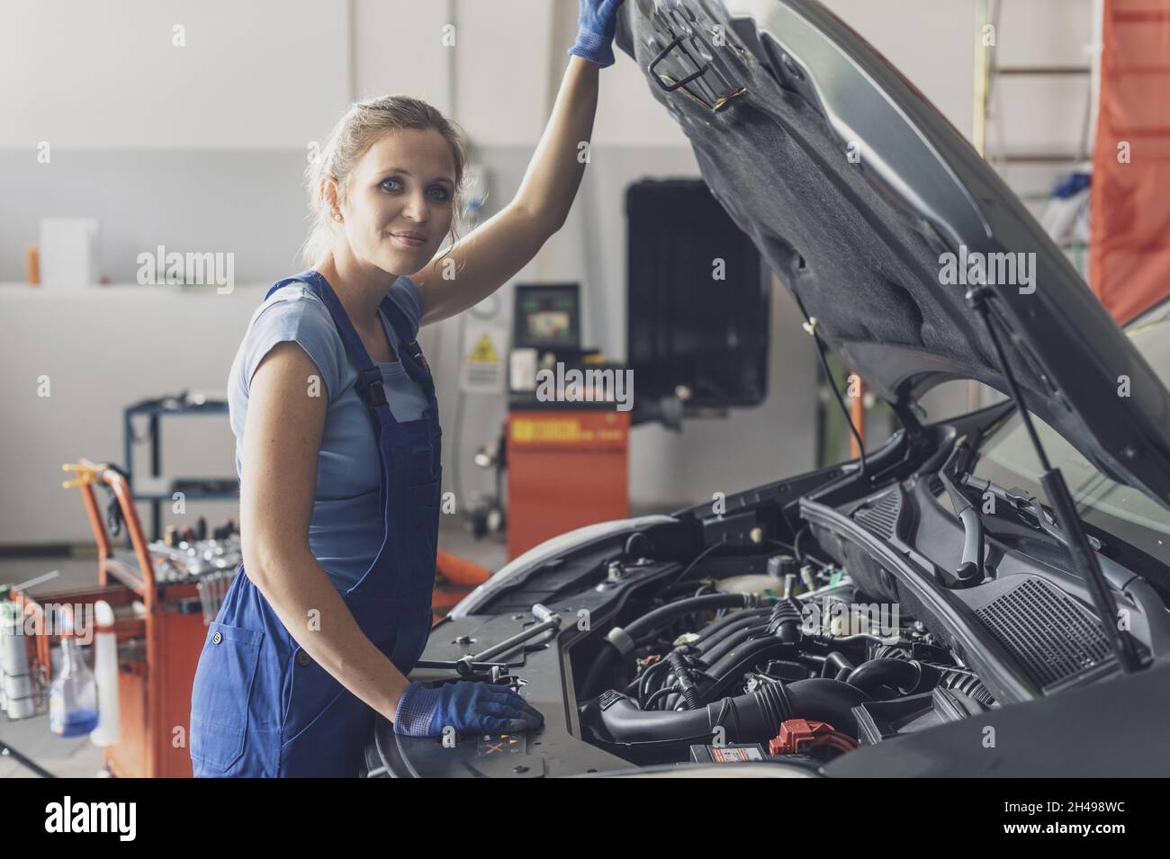 Female mechanic working at the auto repair shop, she is checking a car ...