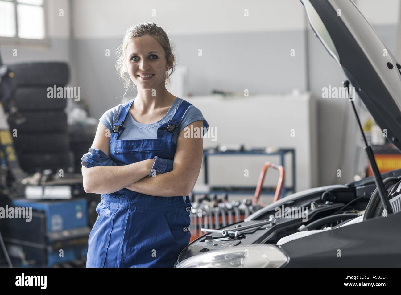 Smiling female mechanic posing next to a car with hood up, women's ...