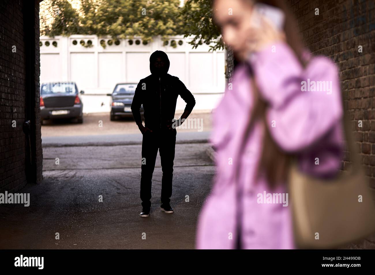 Criminal stalking a woman alone in dark street alley. Female is talking ...