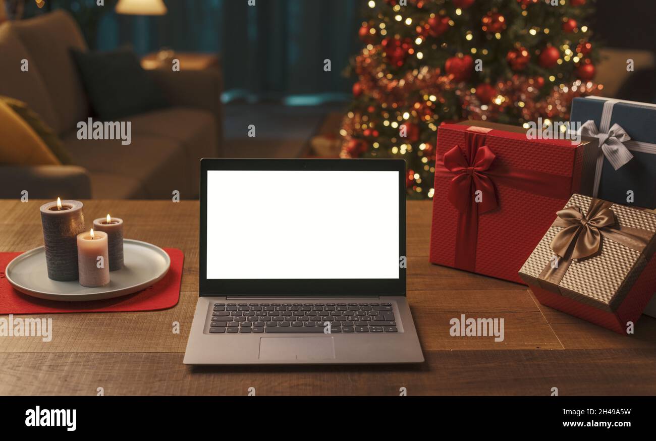 Laptop with blank screen on a table with gifts, Christmas tree in the ...