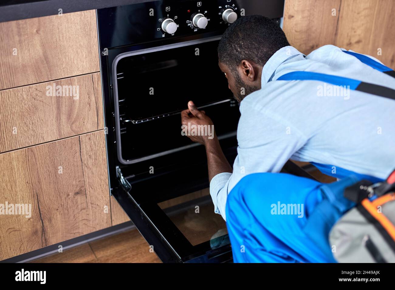 African Handyman Examining Electric Oven In Kitchen At Home. Appliance ...