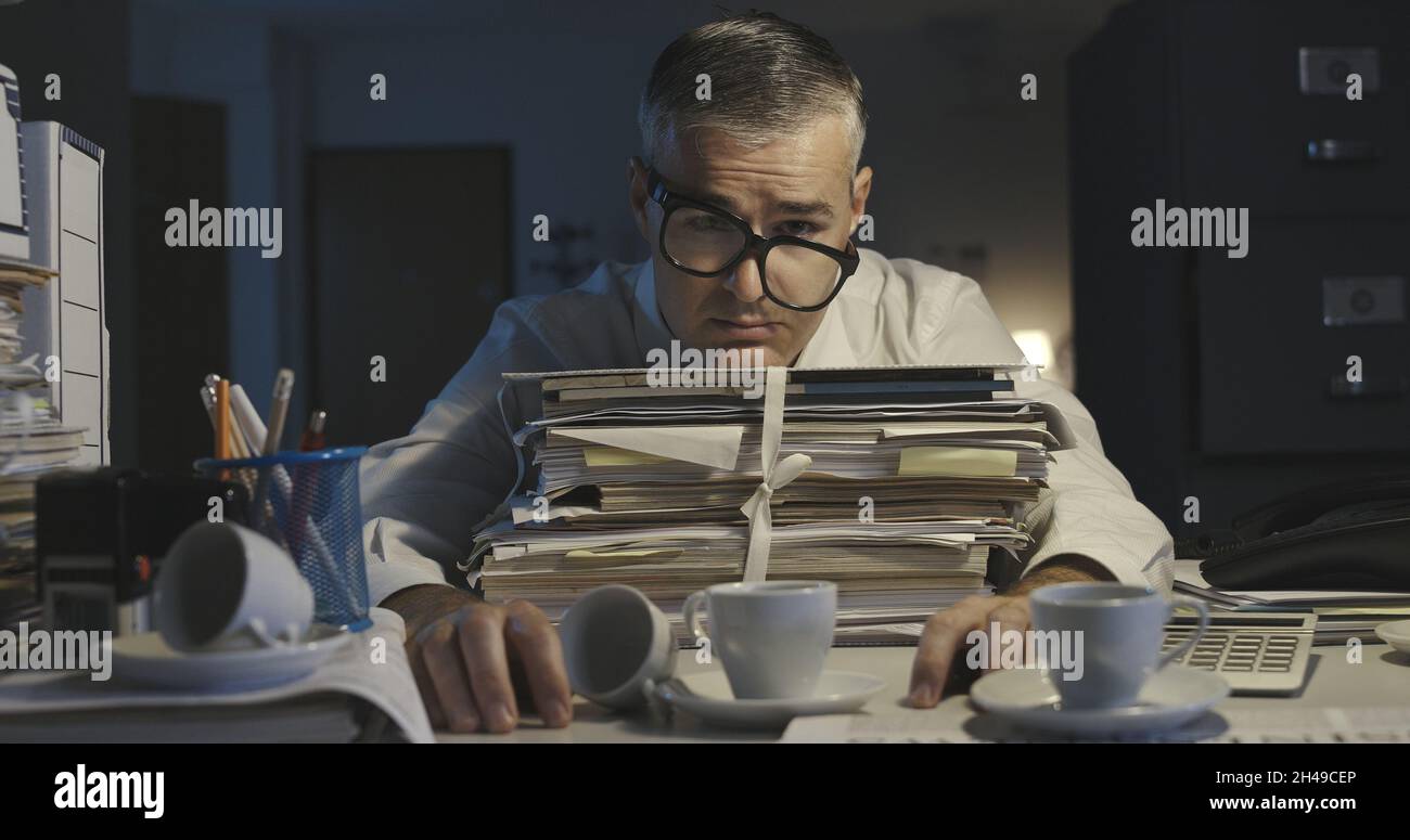 Sad office worker sitting at desk and working overtime at night, he is ...